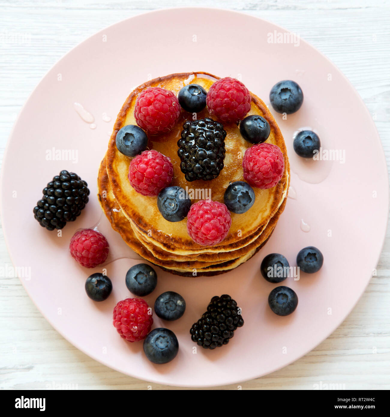 Top view, pancakes with berries and honey on a pink plate. Overhead ...