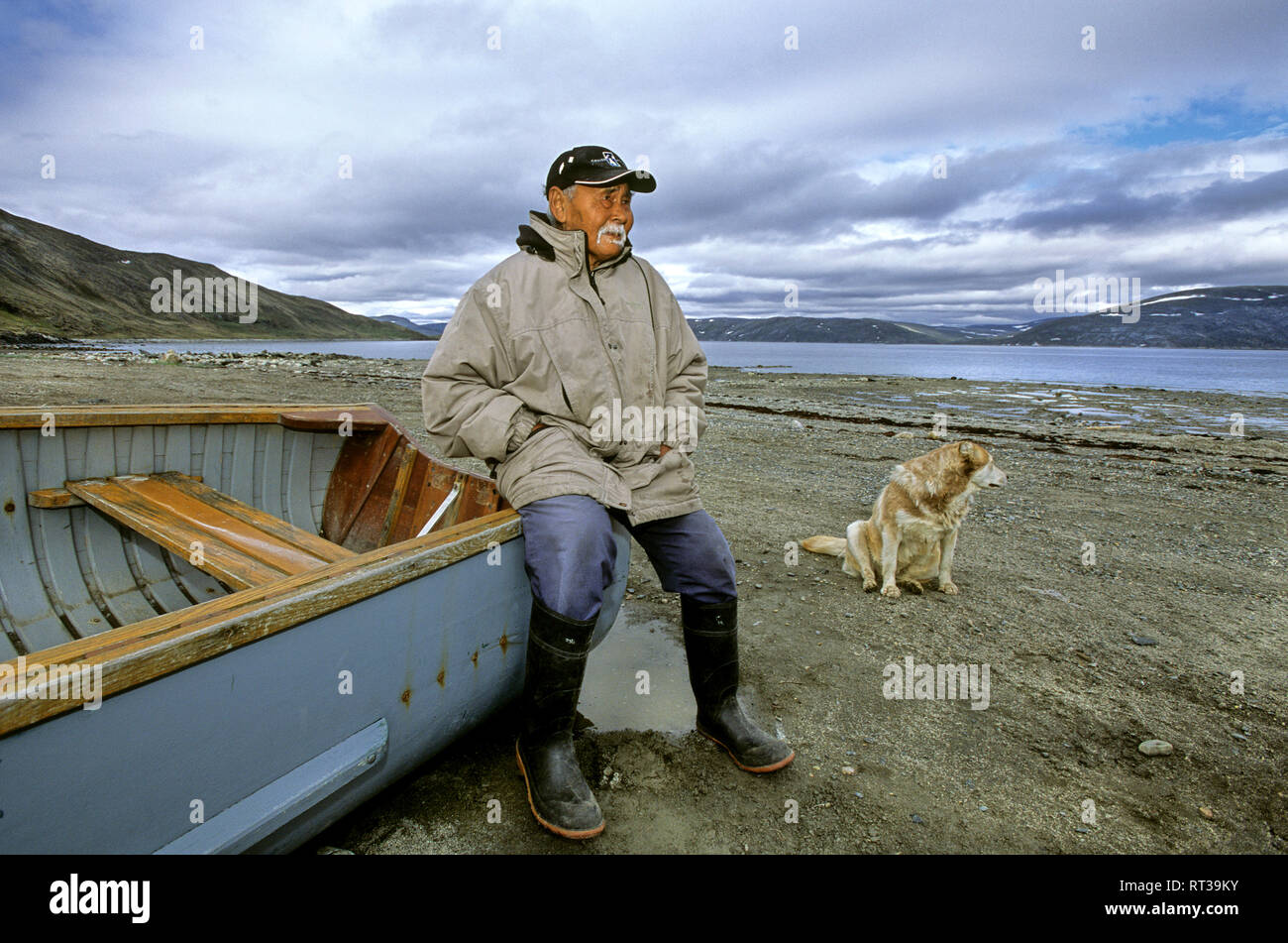 Old Inuit man sitting with his dog in Kangiqsujuaq at the Hudson Bay in ...