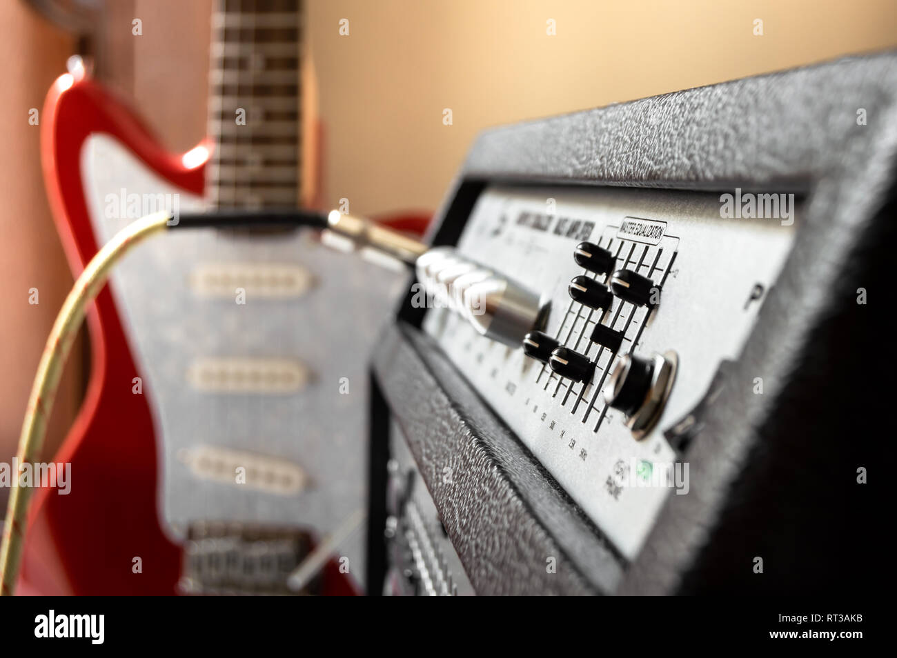 Red electric guitar plugged into large speaker. Close up of amplifier ...