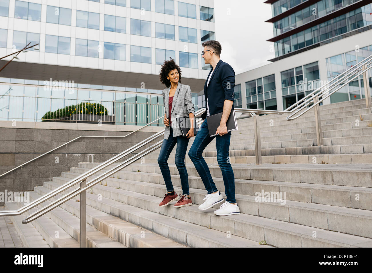 Two colleagues walking and talking on stairs outside office building in ...