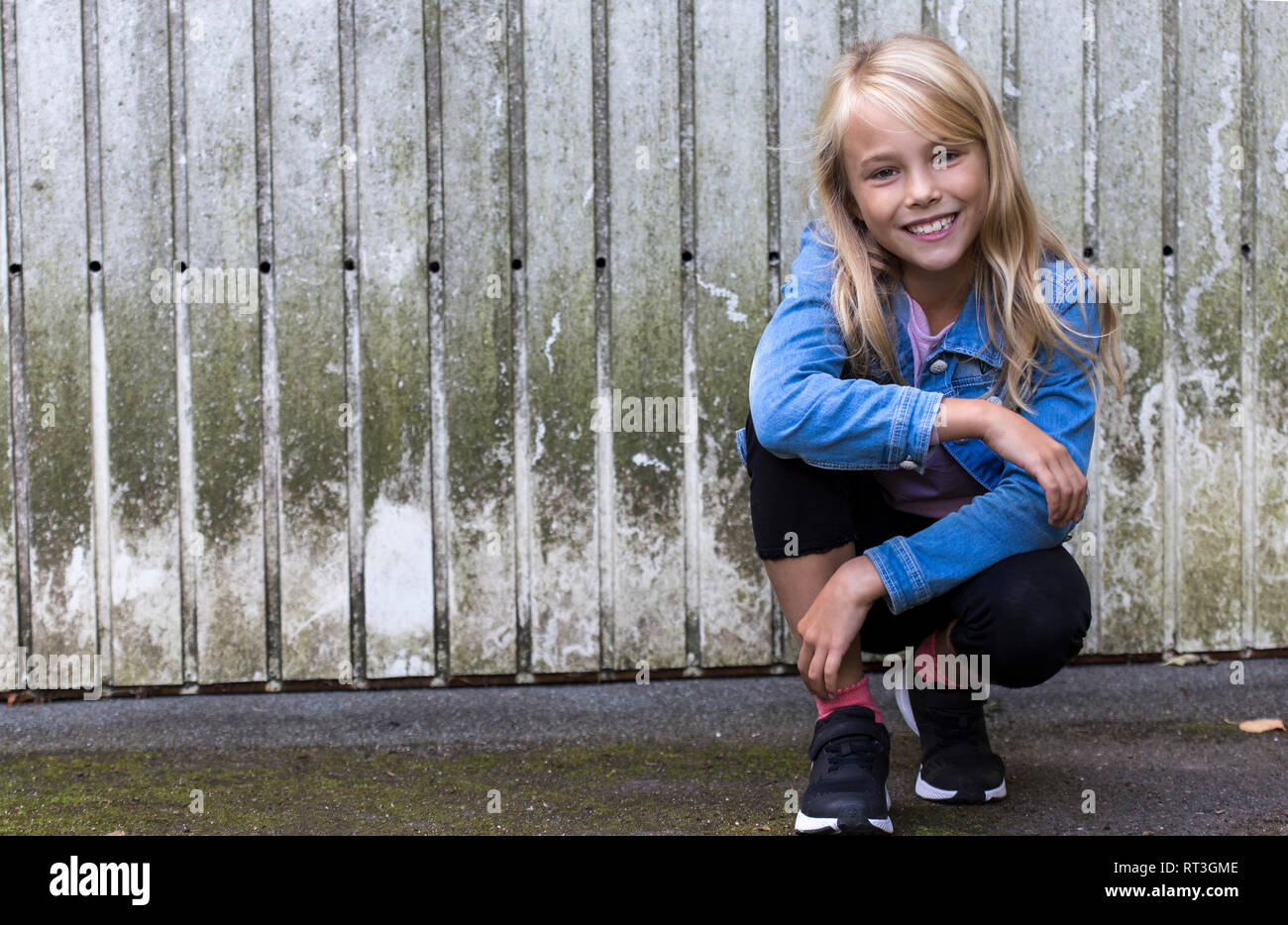 Portrait smiling blond girl crouching front wooden wall hi-res stock ...