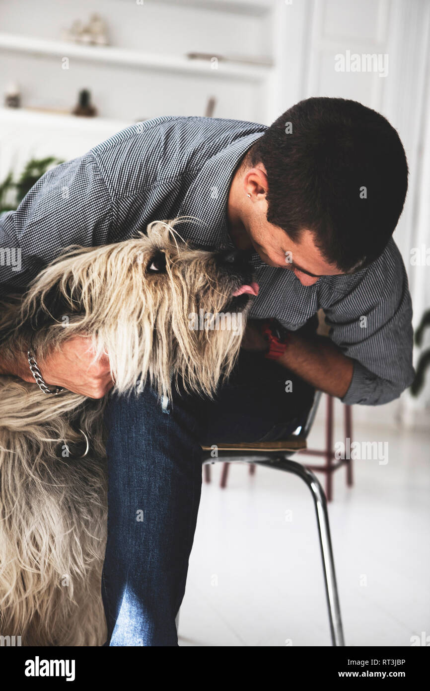 Young man sitting on chair cuddling dog Stock Photo - Alamy