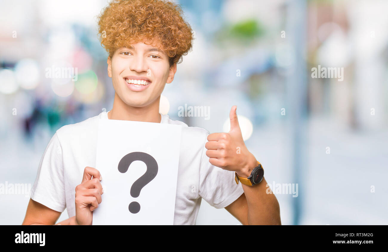 Young handsome man holding paper with question mark happy with big ...