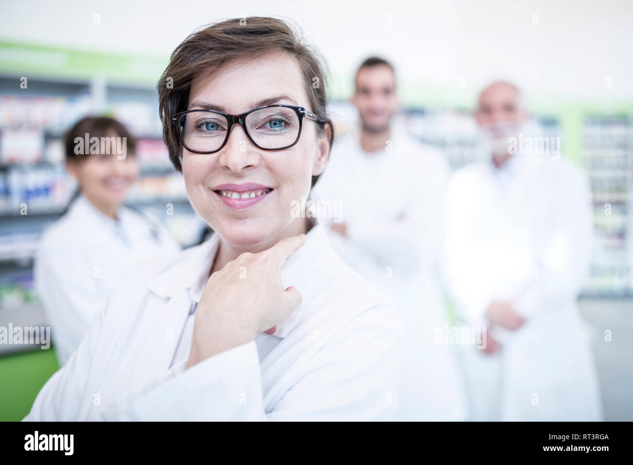 Portrait of smiling pharmacist in pharmacy with colleagues in ...