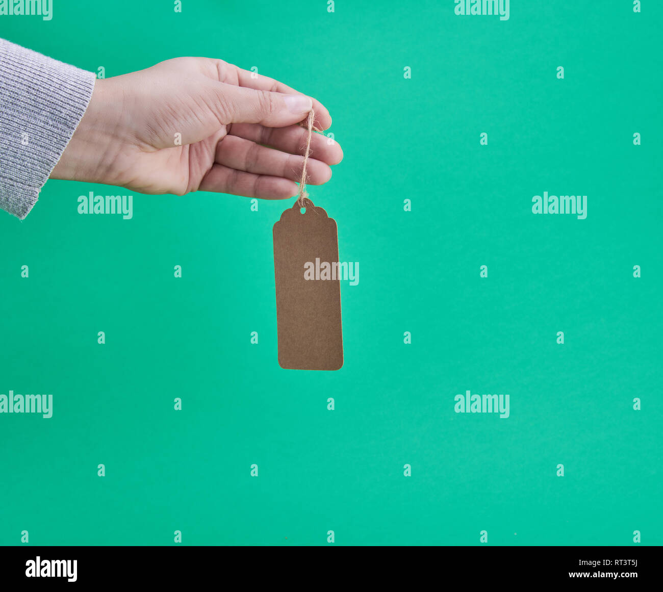 female hand holding a paper brown blank tag on a rope,green background ...