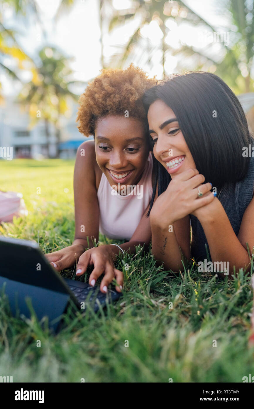 Portrait of two happy female friends relaxing in a park using a tablet ...
