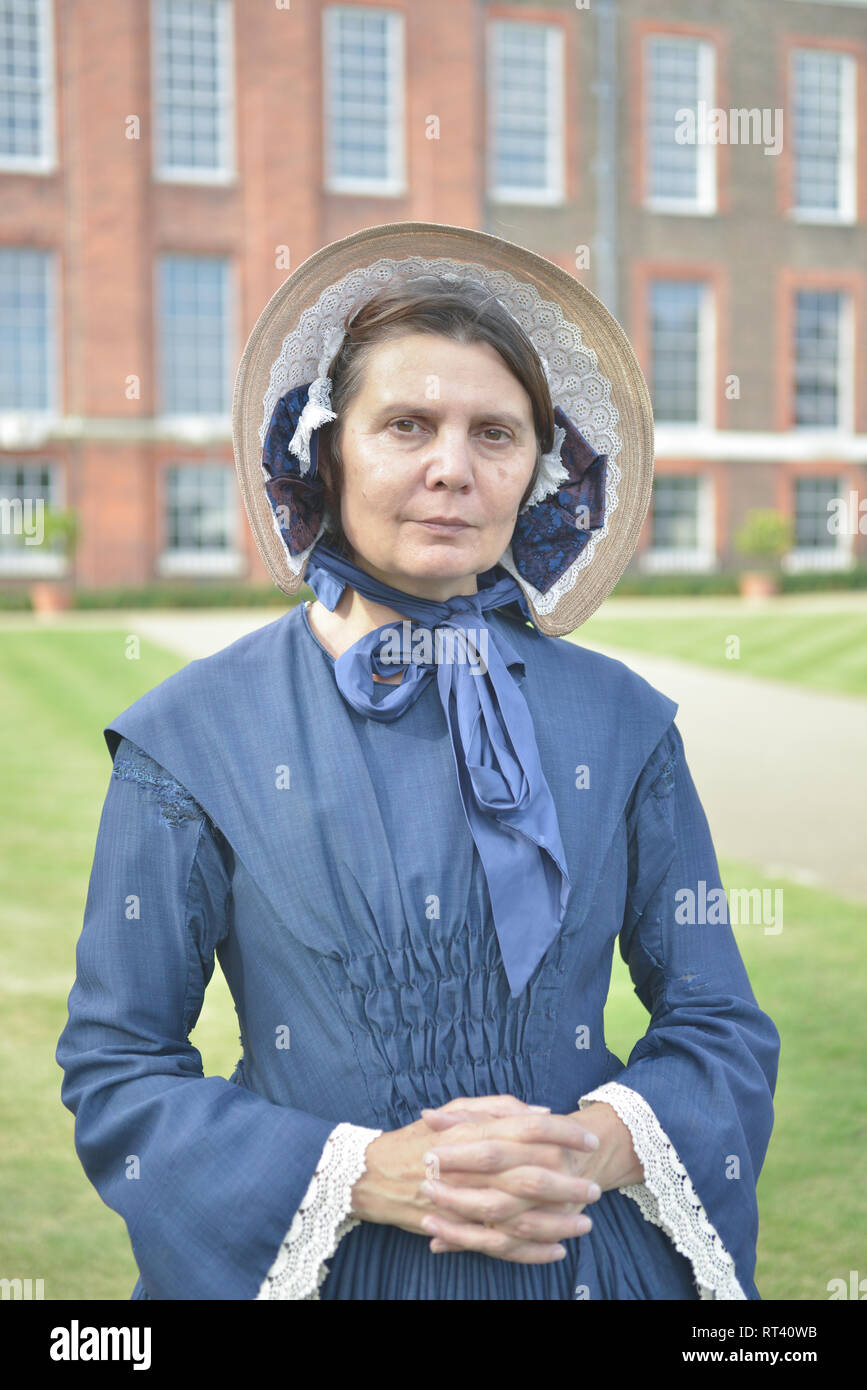 An old stern looking Victorian woman in a bonnet stands in front of ...