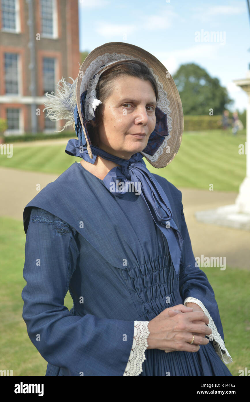 An old stern looking Victorian woman in a bonnet stands in front of ...