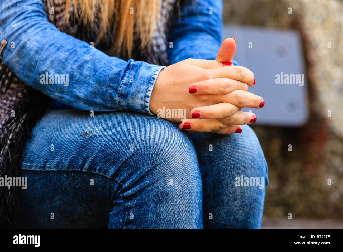 Hands gesture. Woman wearing jeans waiting for someone sitting on bench ...