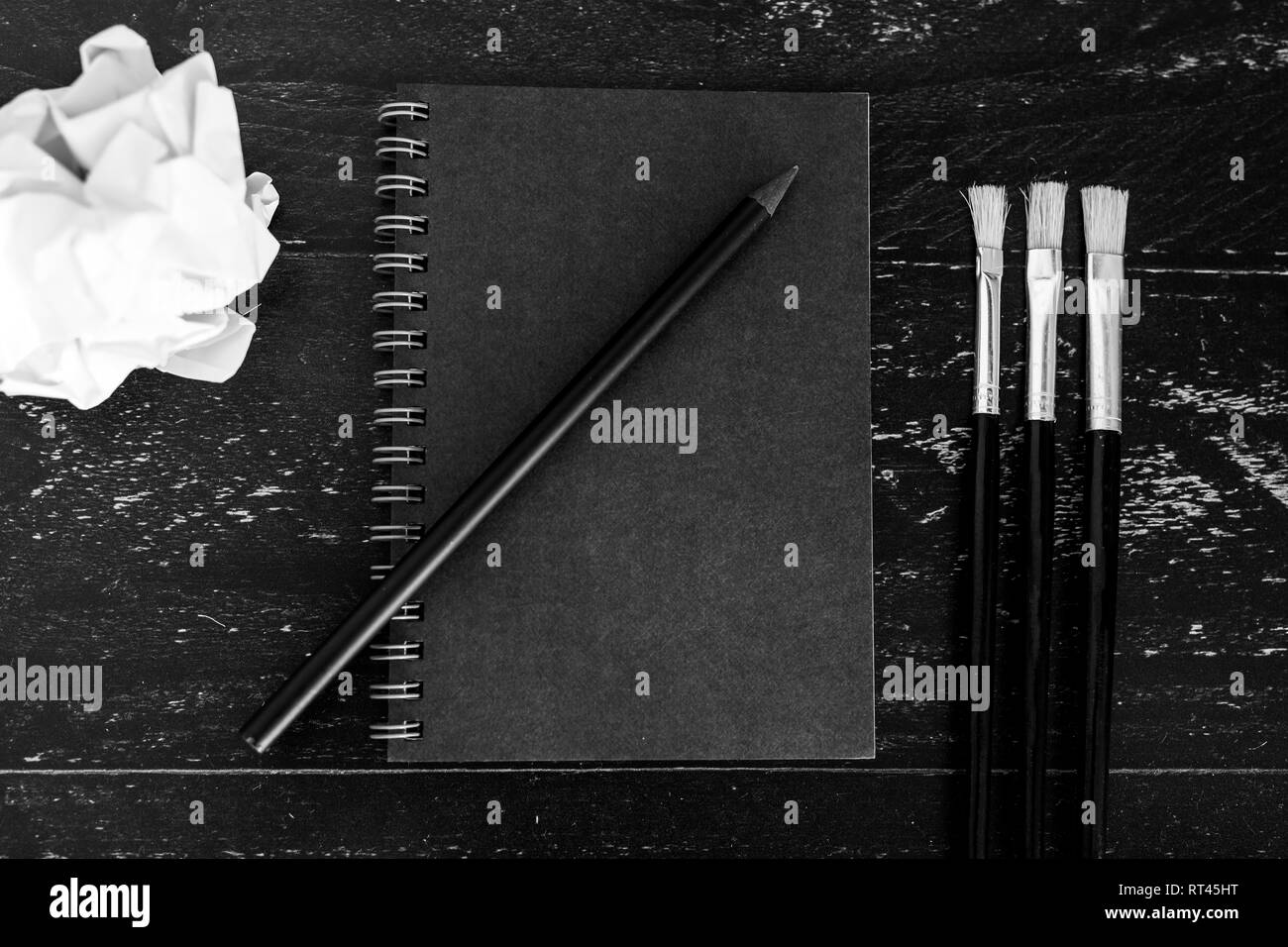 black notepad on dark desk with brushes and scrunched paper balls ...