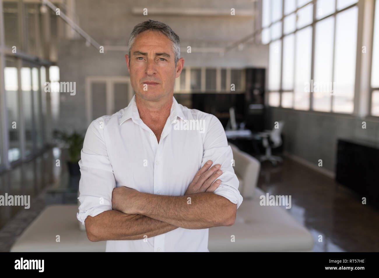 Male executive standing with arms crossed in office Stock Photo - Alamy