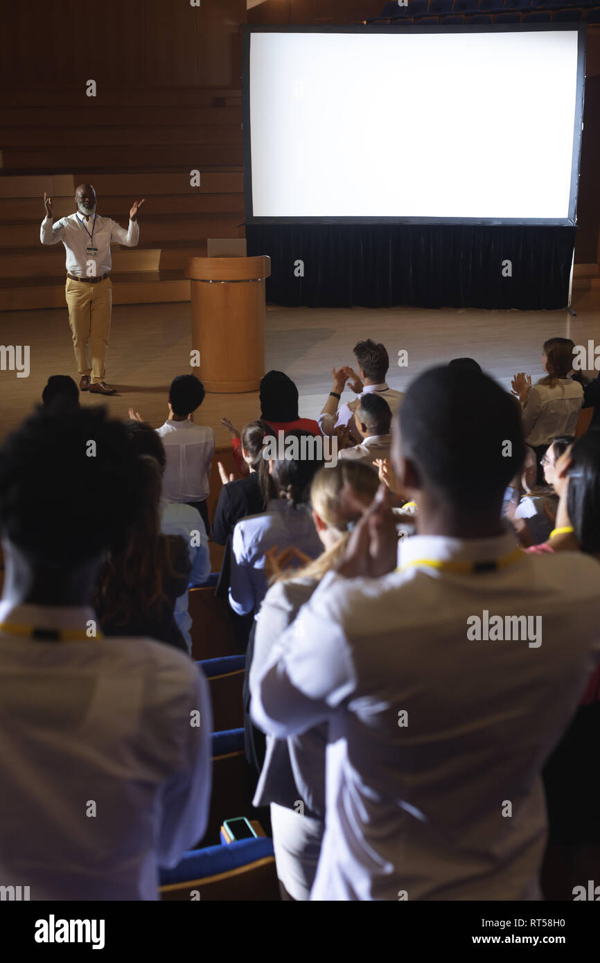Businessman standing and giving presentation in auditorium Stock Photo ...