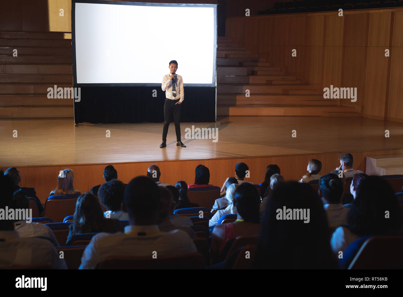Businessman standing and giving presentation in auditorium Stock Photo ...