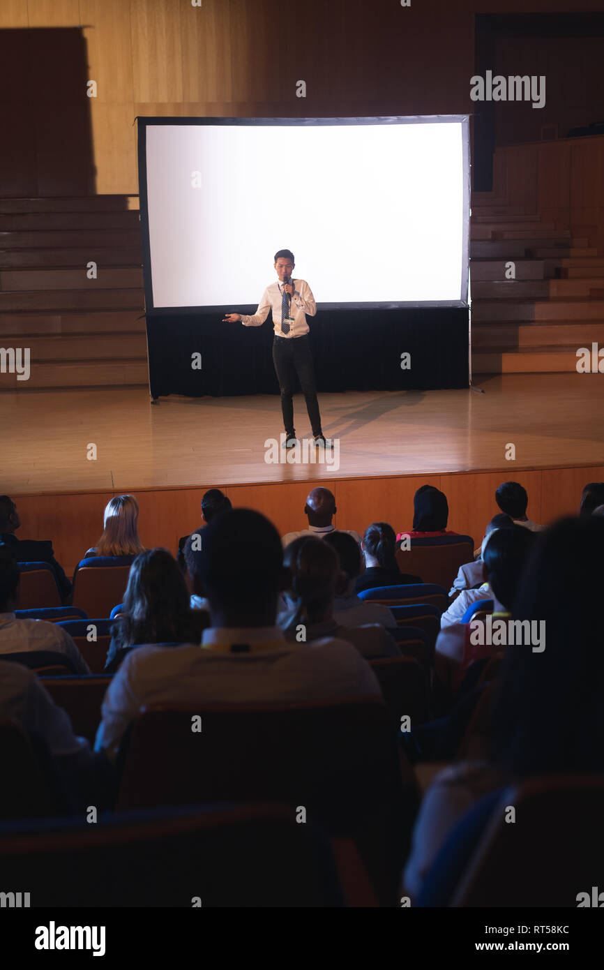 Businessman standing and giving presentation in auditorium Stock Photo ...