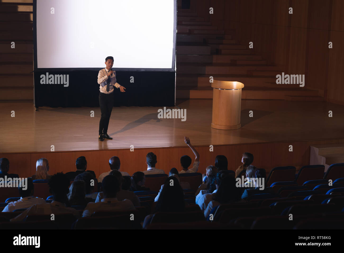 Businessman standing and giving presentation in auditorium Stock Photo ...