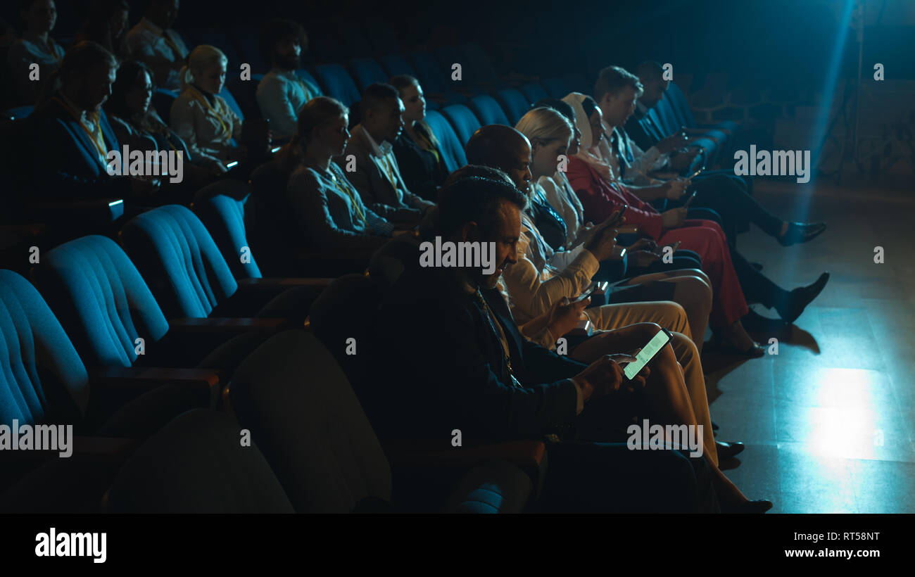 Audience sitting in the auditorium and holding smartphone in their ...