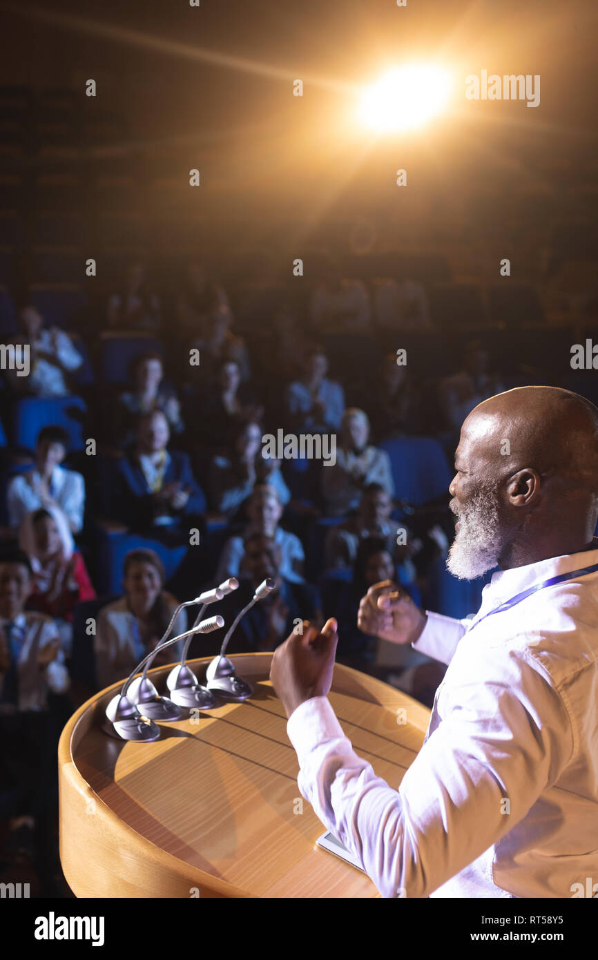 Businessman standing near podium and giving speech to the audience in ...