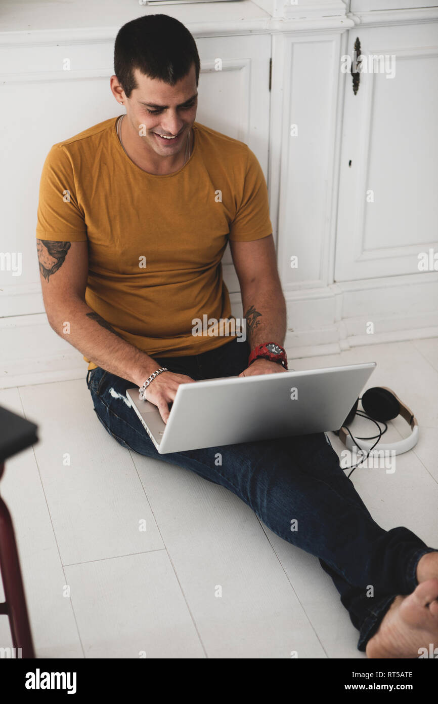 Smiling young man sitting on the floor using laptop Stock Photo - Alamy
