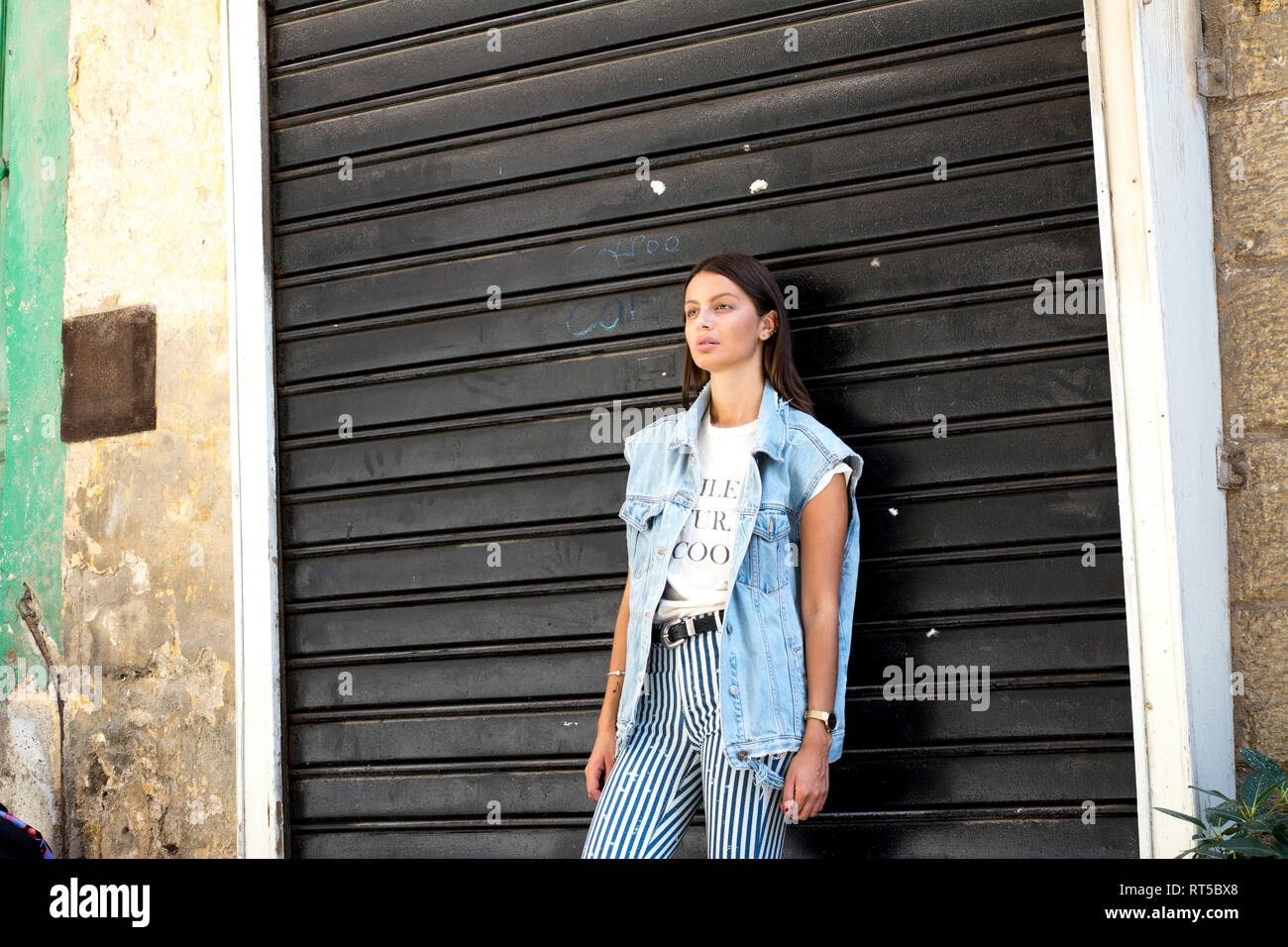 Portrait fashionable young woman standing front roller shutter looking ...