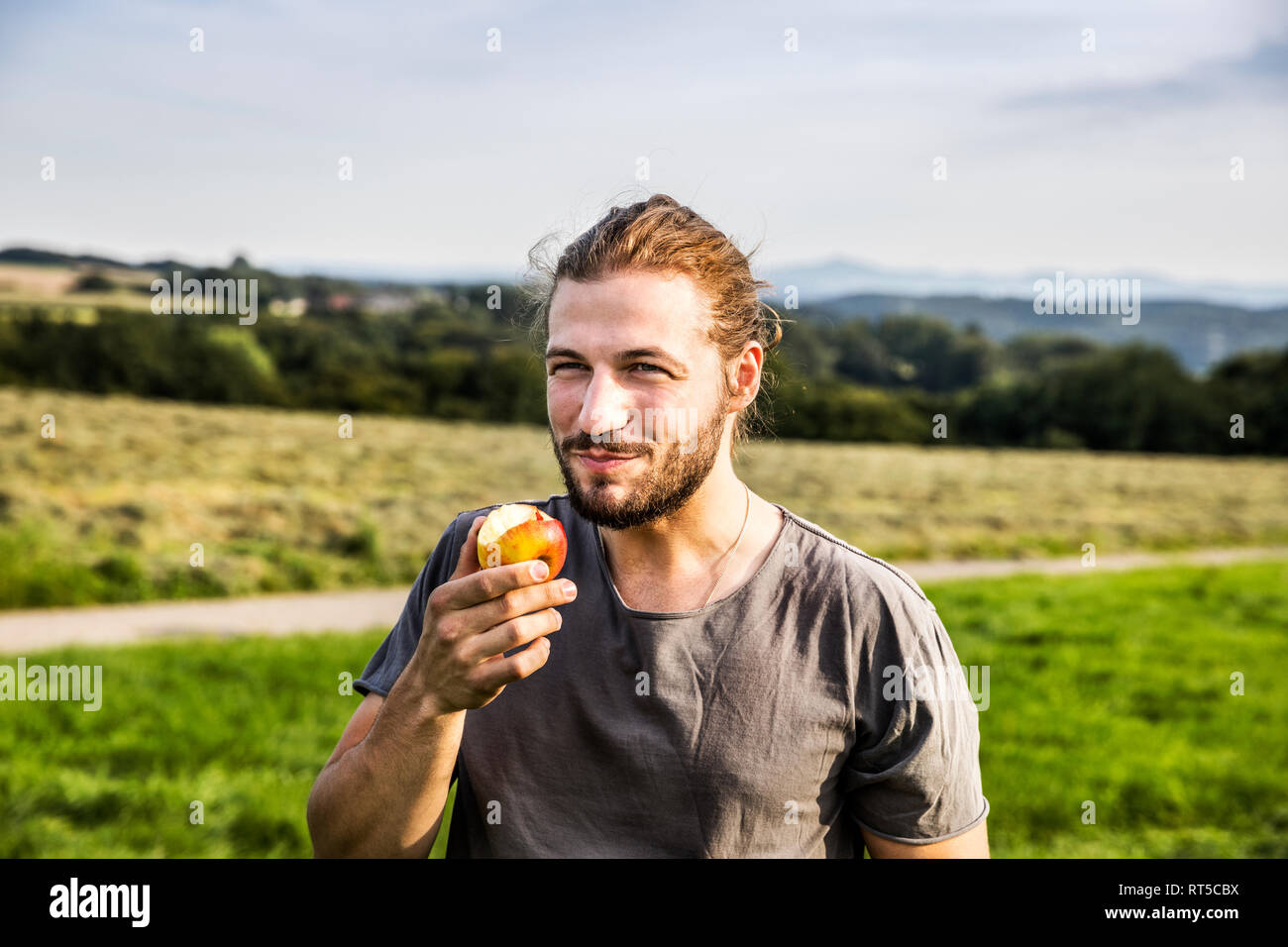 Young man eating an apple in rural landscape Stock Photo - Alamy