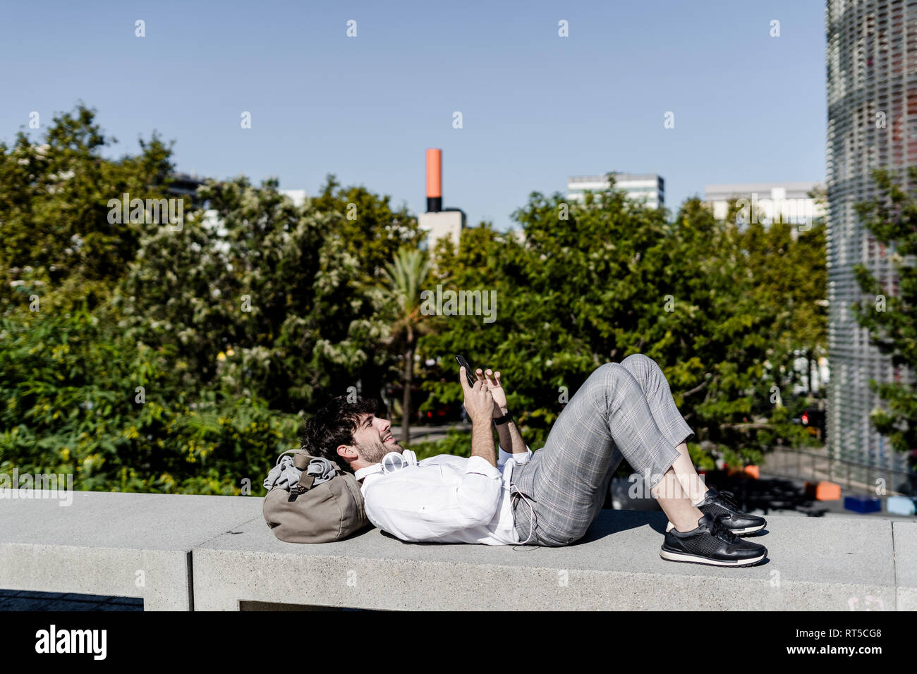 Smiling young man lying on a wall outdoors using cell phone Stock Photo ...