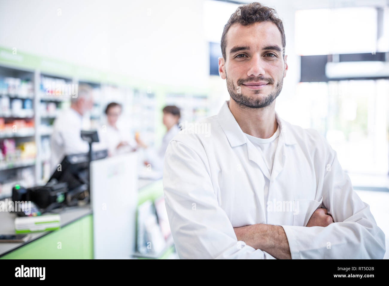 Portrait of smiling pharmacist in pharmacy with colleagues in ...