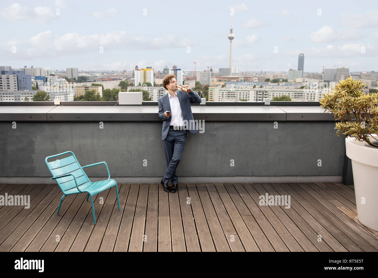 Germany, Berlin, businessman having a drink on roof terrace after work ...