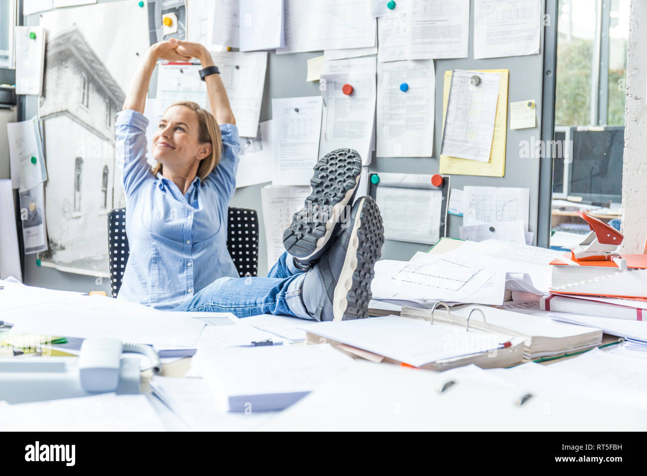 Woman relaxing at desk in office surrounded by paperwork Stock Photo ...