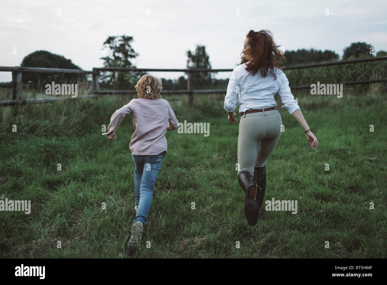 Back view of boy and young woman running side by side on a paddock ...
