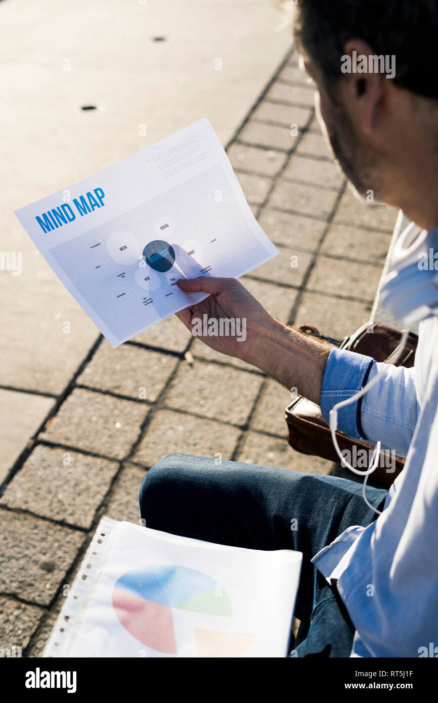 Mature man sitting outdoors holding mind map Stock Photo - Alamy