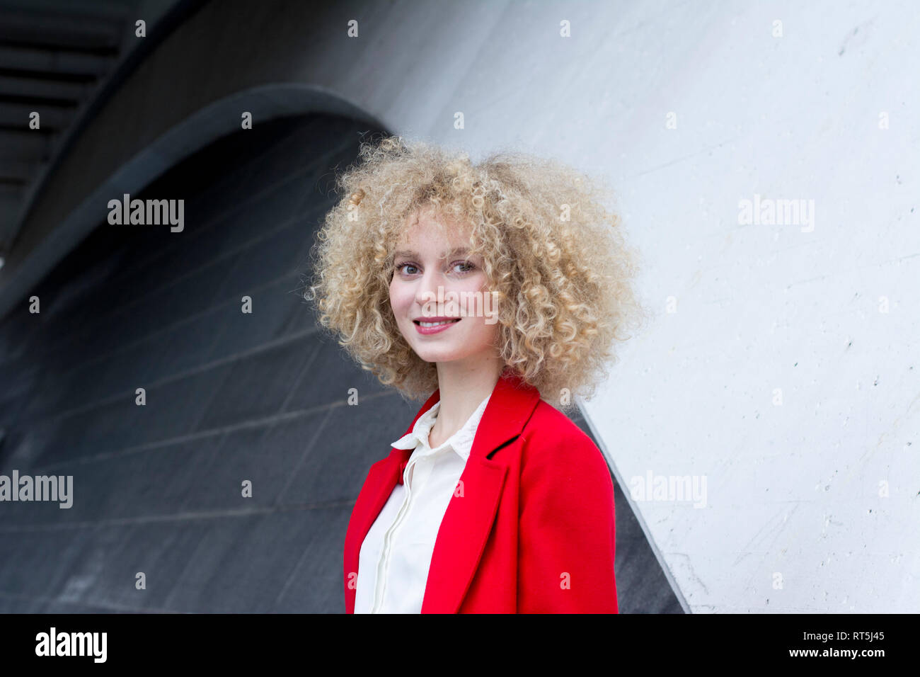 Portrait of smiling blond woman with ringlets wearing red suit coat ...