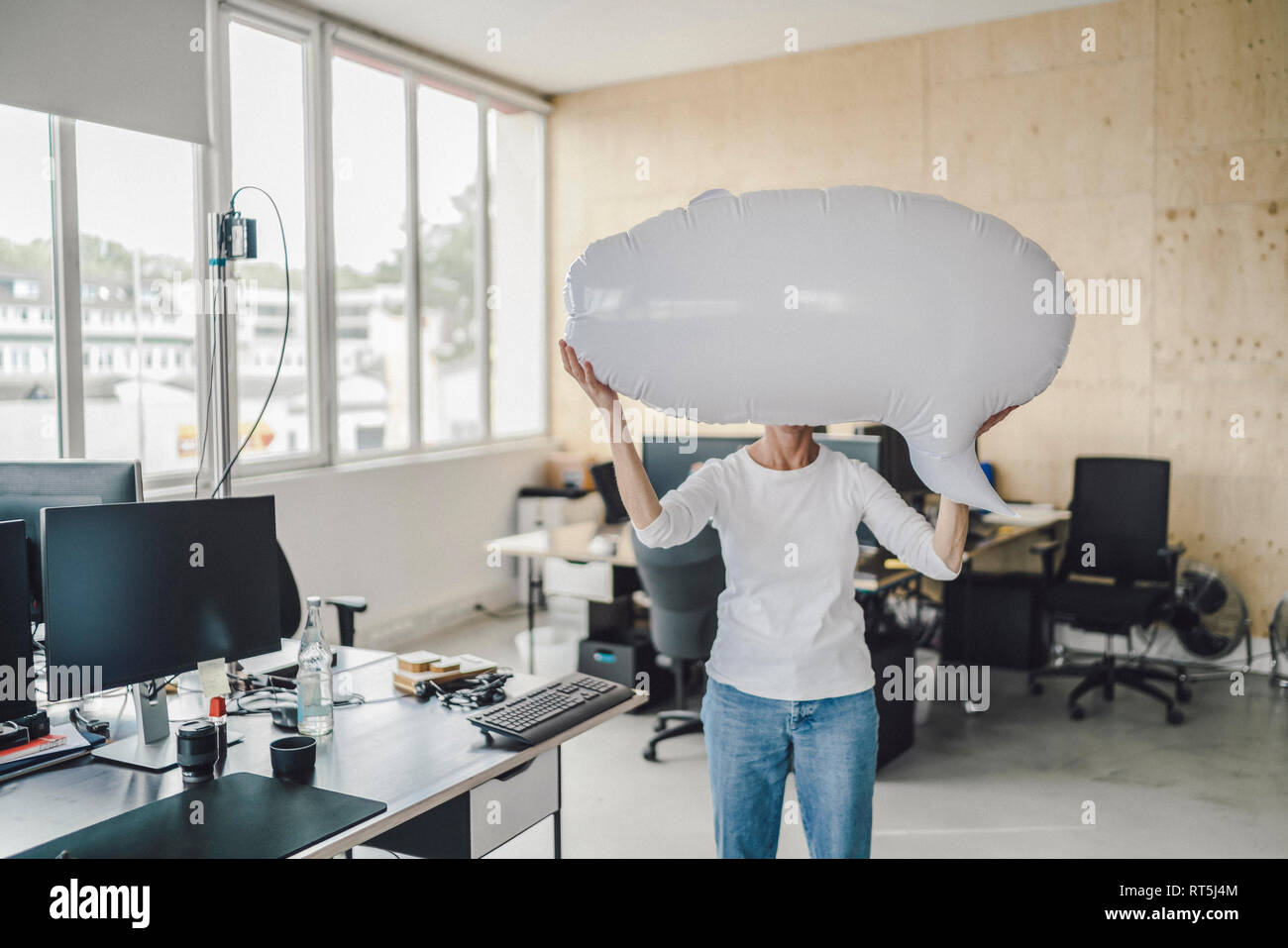 Woman standing in office, holding inflatable speech bubble in front of ...