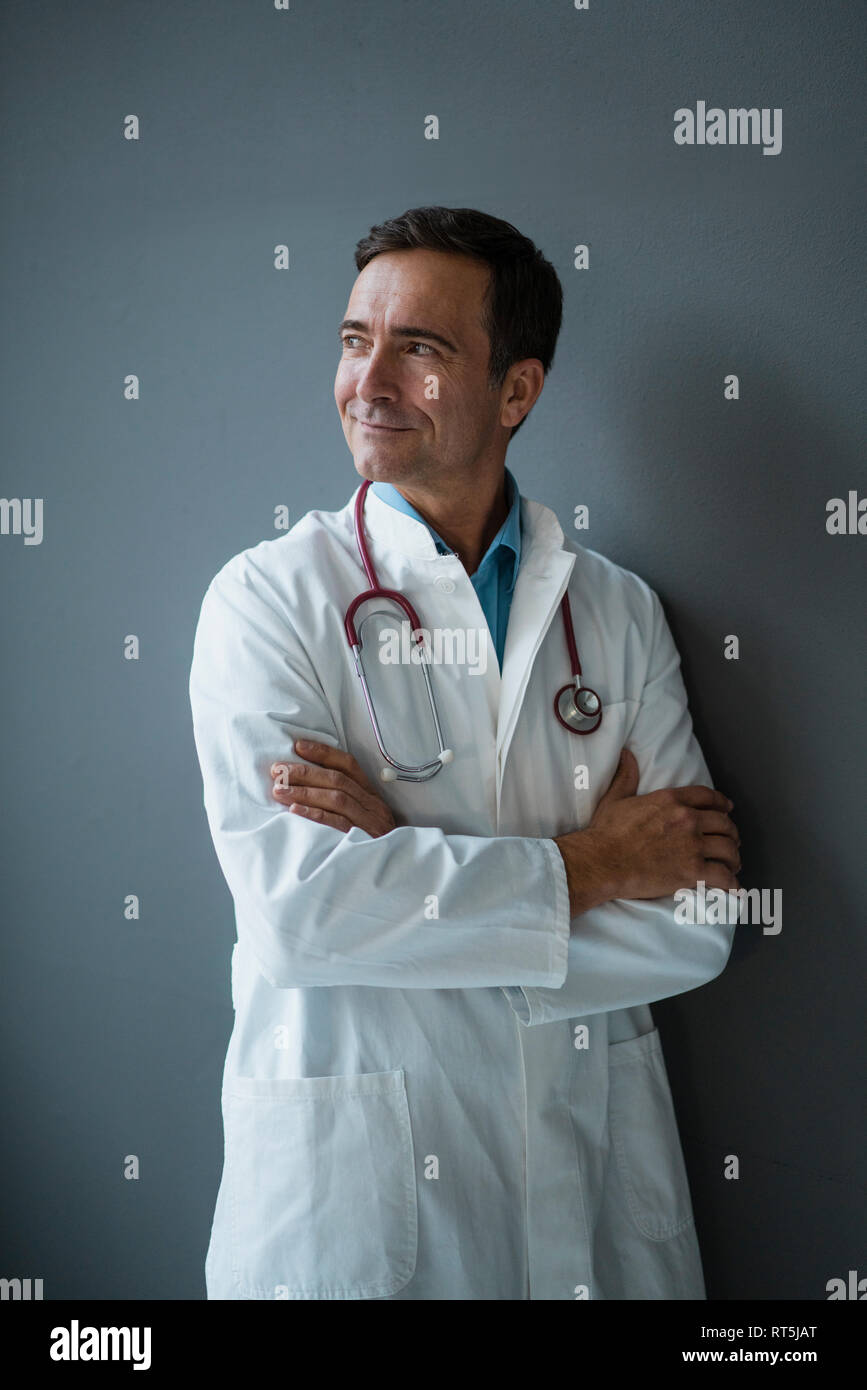 Smiling doctor standing at a grey wall looking sideways Stock Photo - Alamy