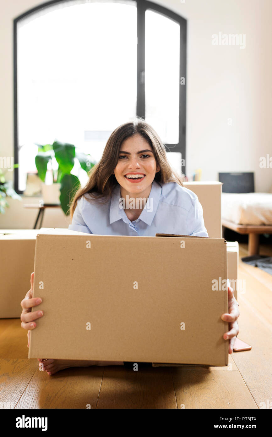 Portrait of smiling young woman holding cardboard box in new apartment ...