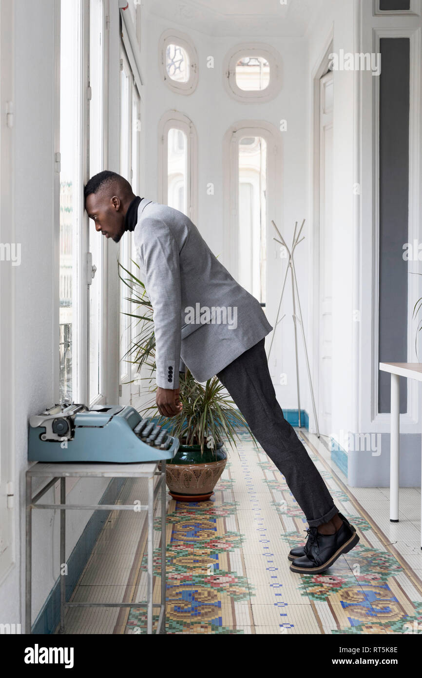 Young businessman in office leaning with forehead against window ...