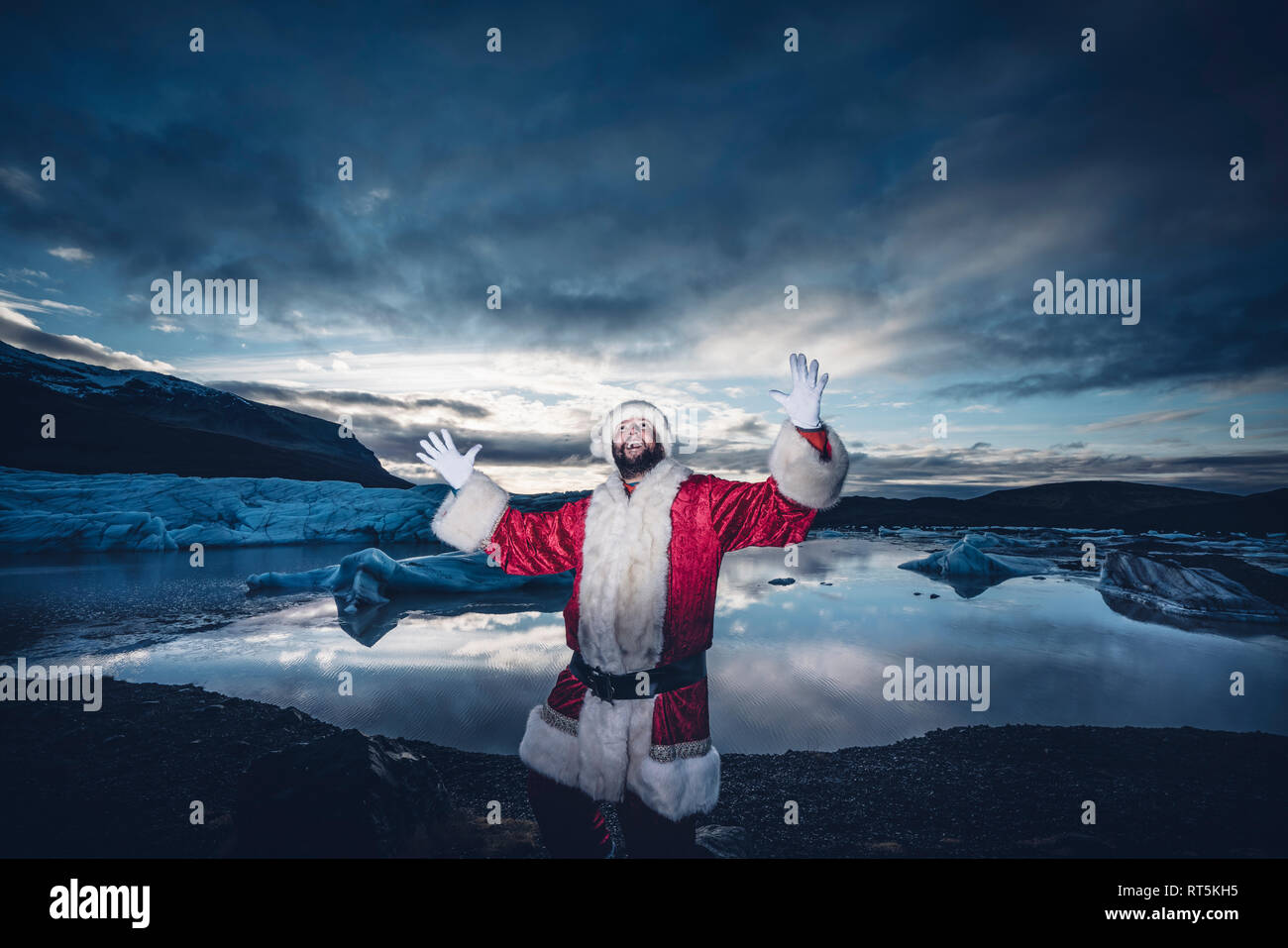 Iceland, man disguised as Santa Claus standing at a glacier raising his ...