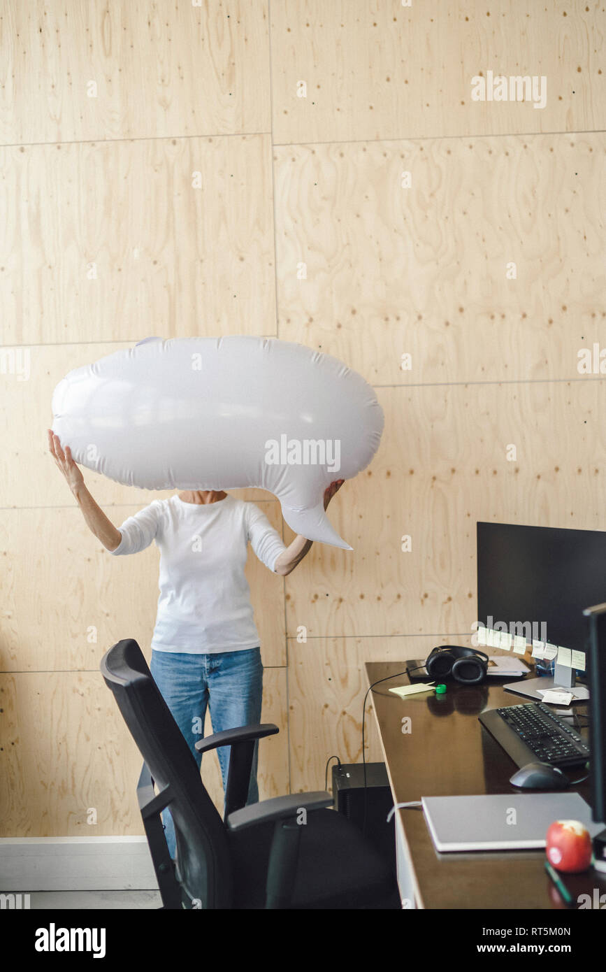 Woman standing in office, holding inflatable speech bubble in front of ...