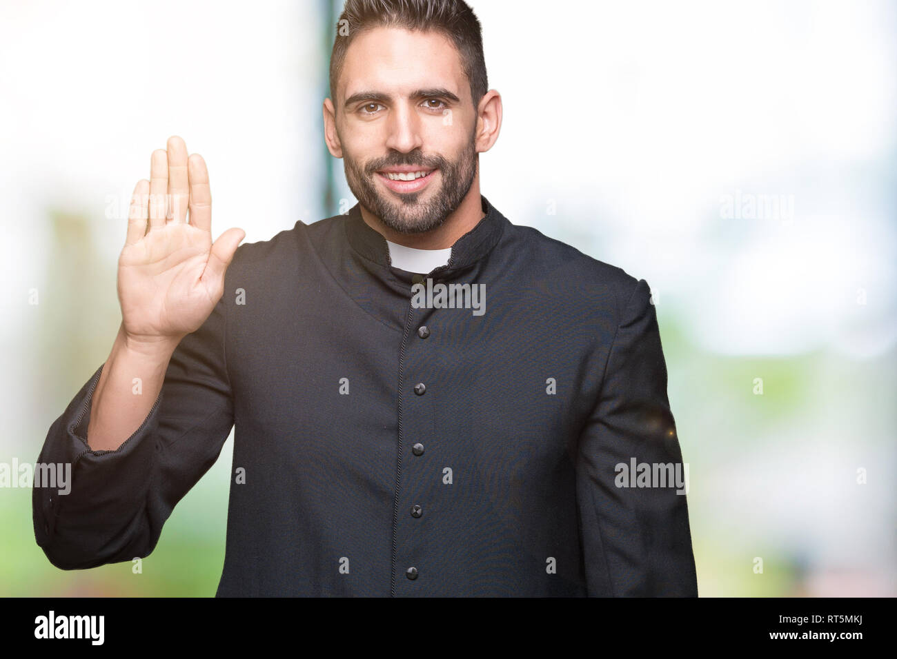 Young Christian priest over isolated background Waiving saying hello ...