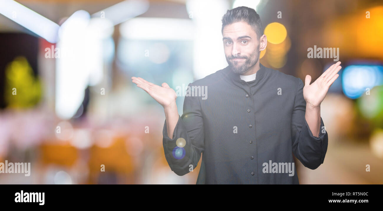 Young Christian priest over isolated background clueless and confused ...