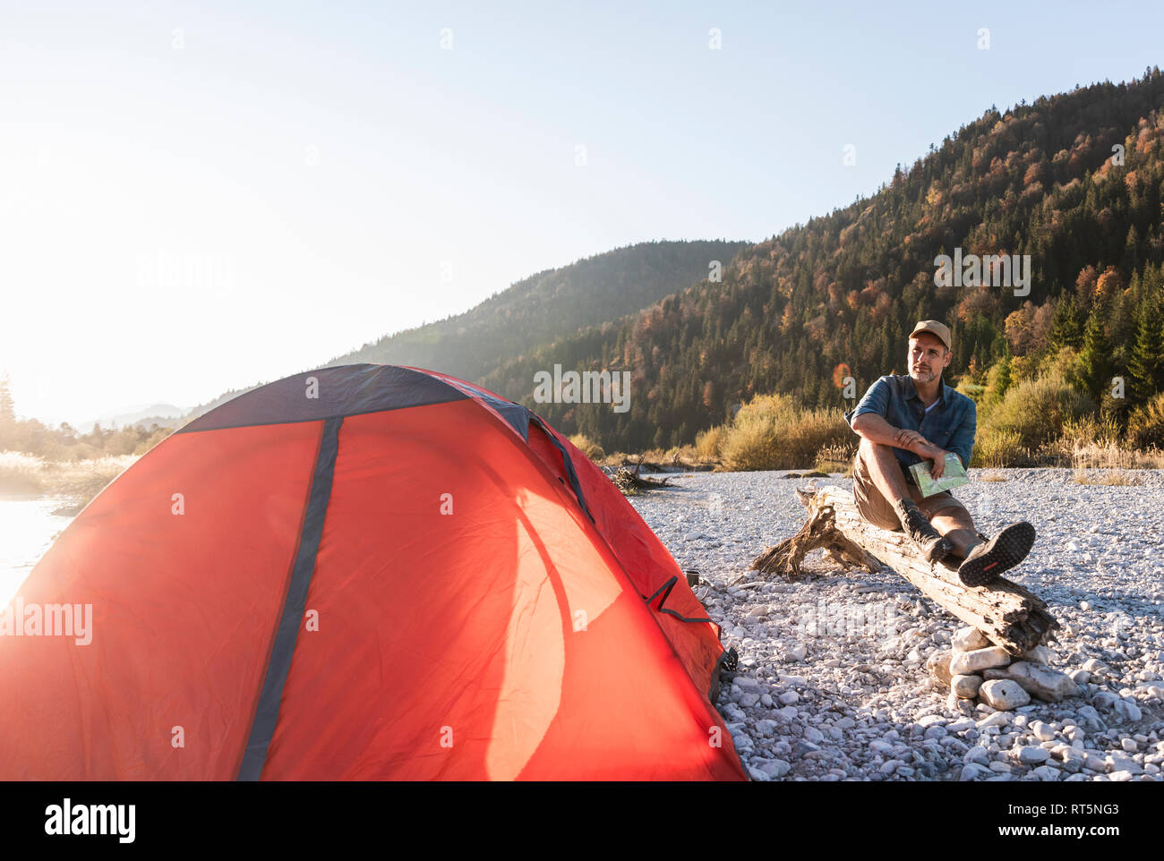 Mature man camping at riverside, sitting on tree trunk with map Stock ...