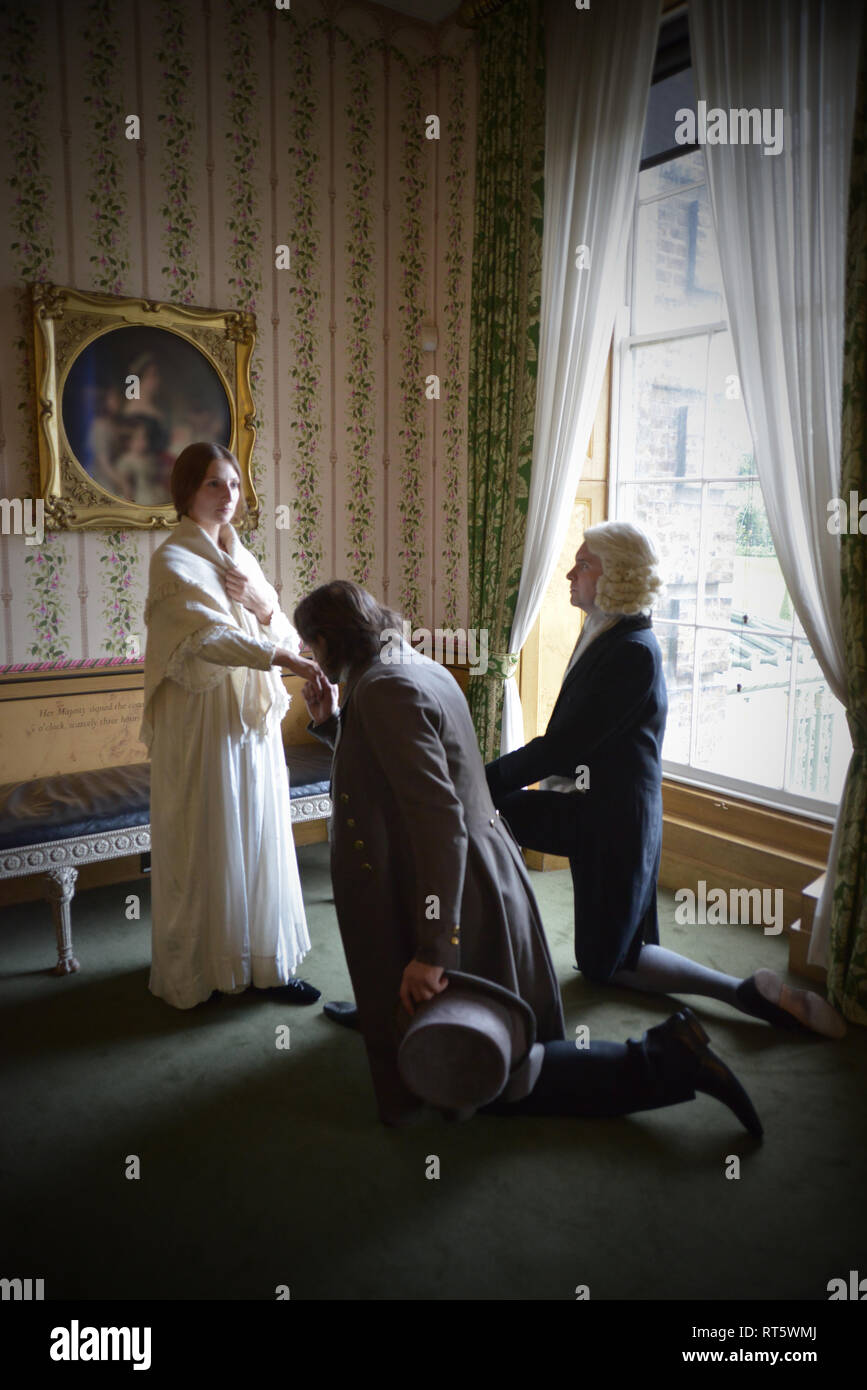 Two men in Victorian dress kneel before a young Princess Victoria to ...