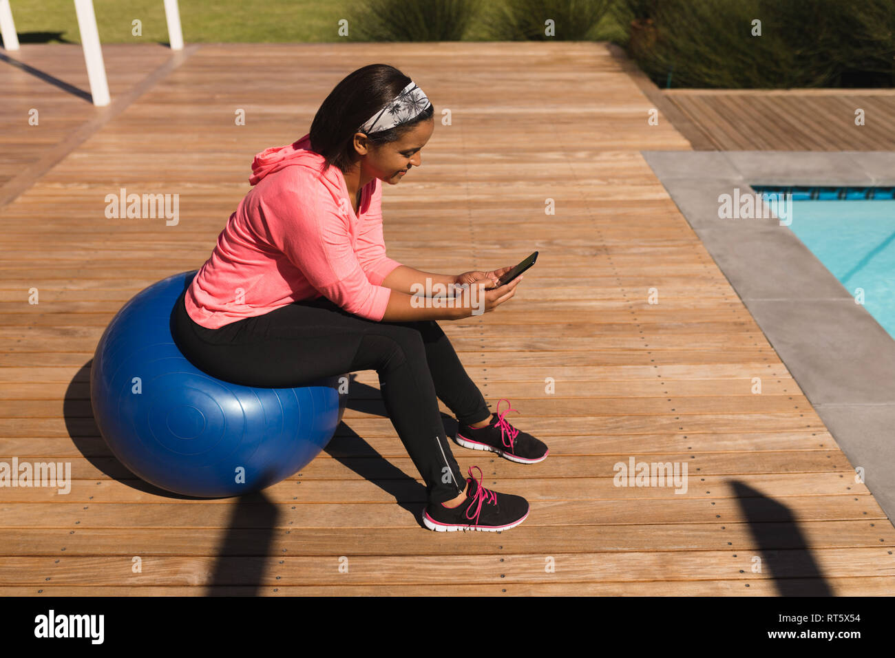 Woman using mobile phone while sitting on exercise ball in the backyard ...