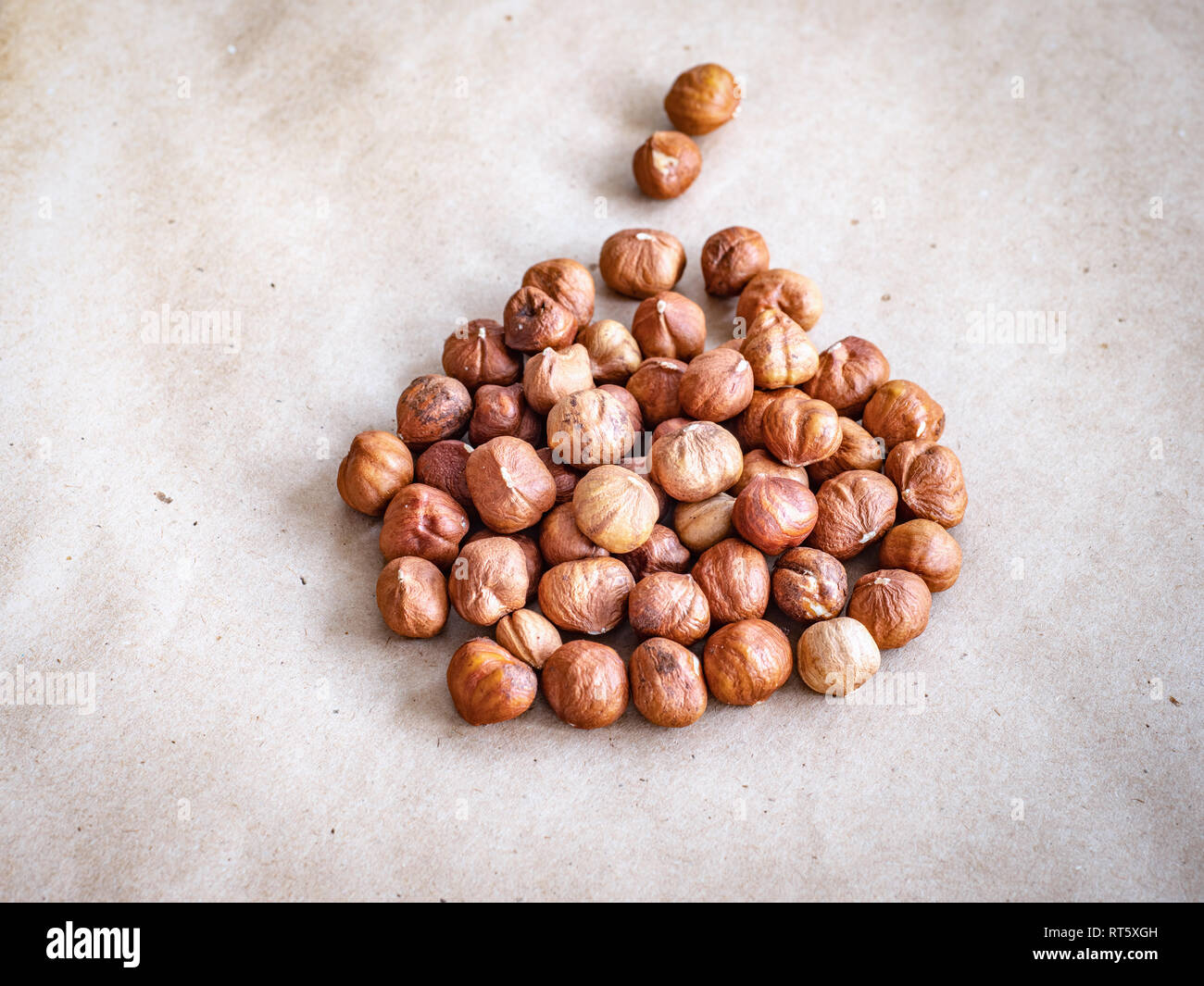 A handful of peeled hazelnut kernels are scattered on coarse craft ...