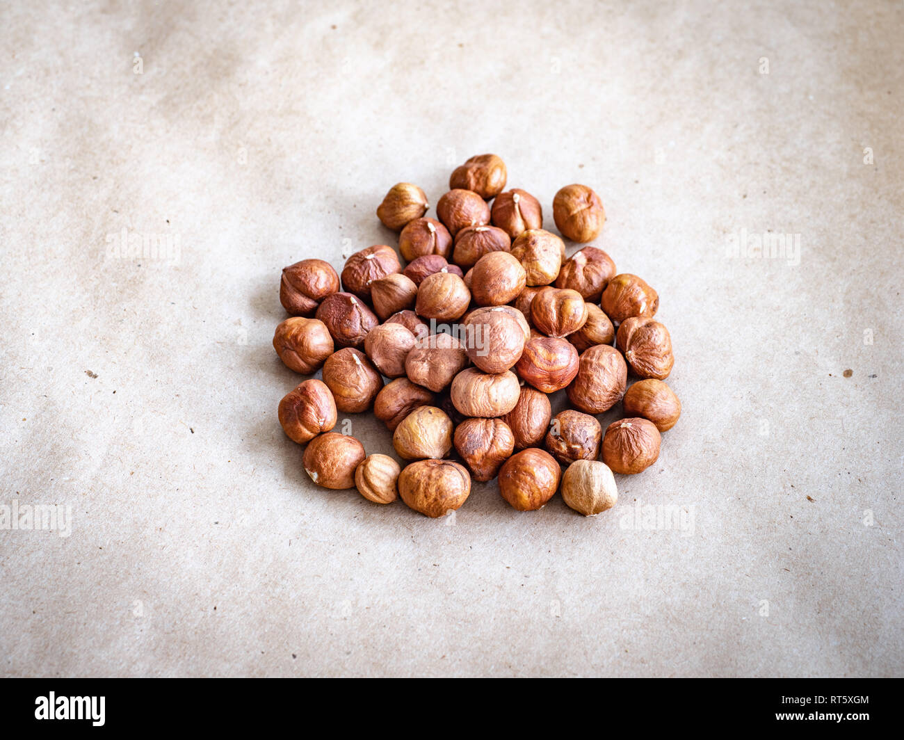 A handful of peeled hazelnut kernels are scattered on coarse craft ...