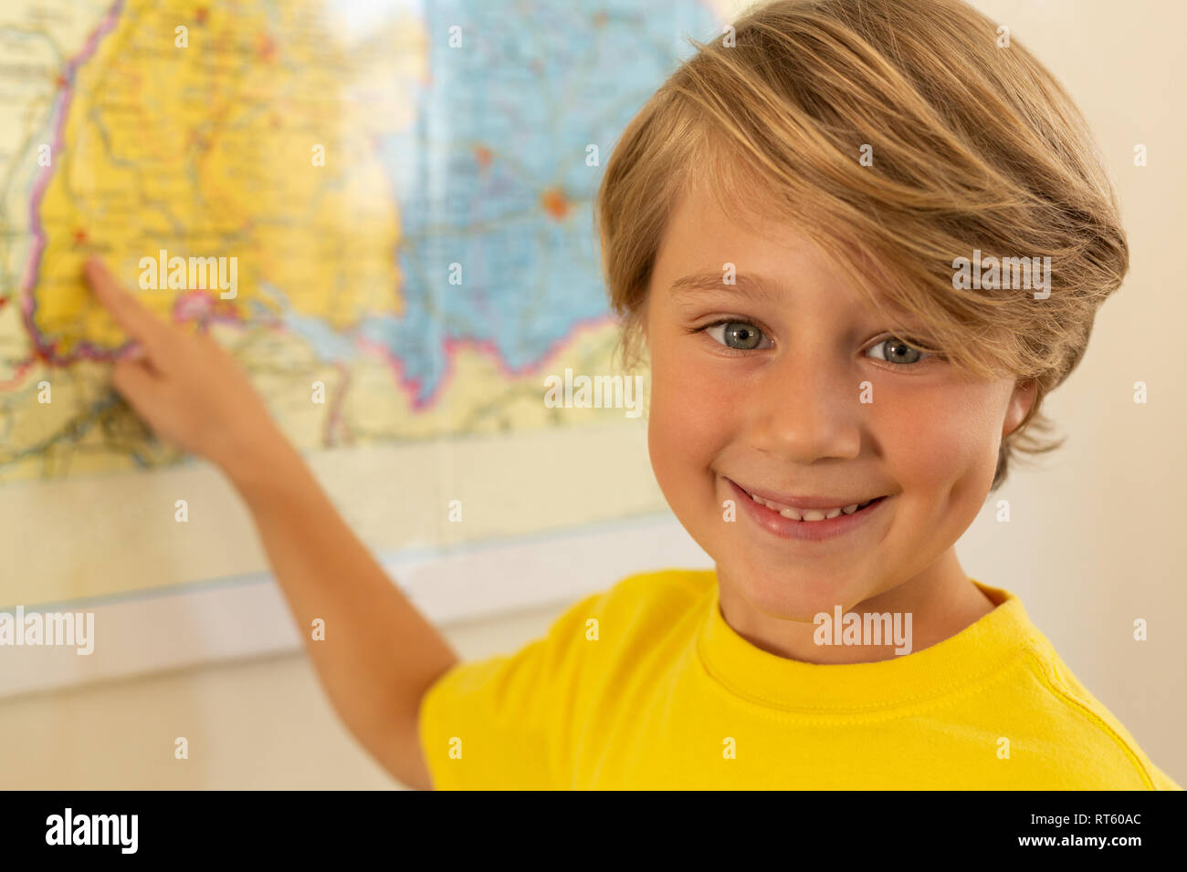 Happy boy looking at camera and pointing with his finger on a map in ...