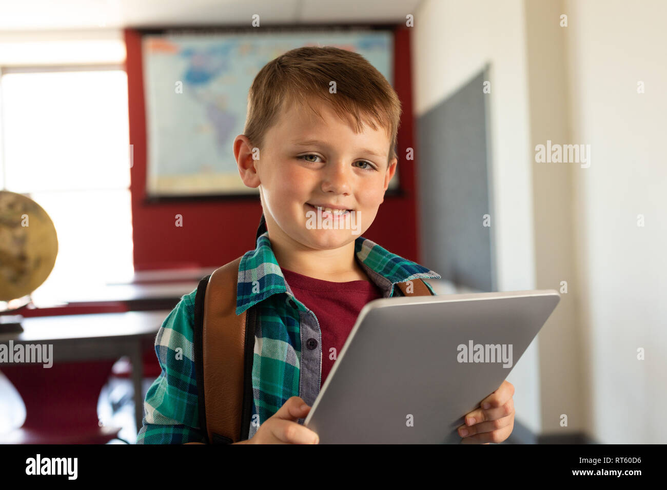 Happy boy with school bag and digital tablet looking at camera in a ...