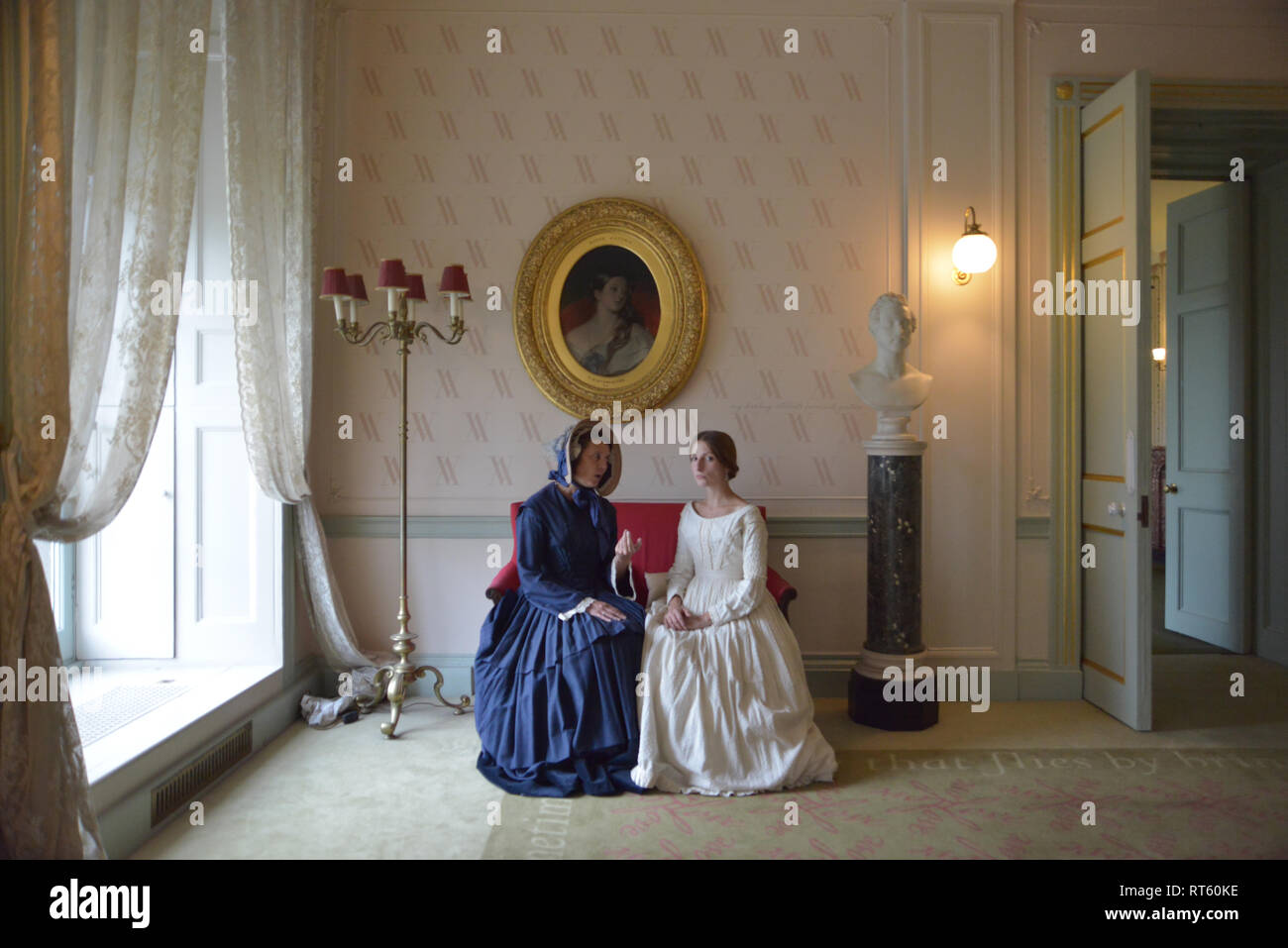 Two Women in Victorian dresses sit and chat in a formal parlour at ...