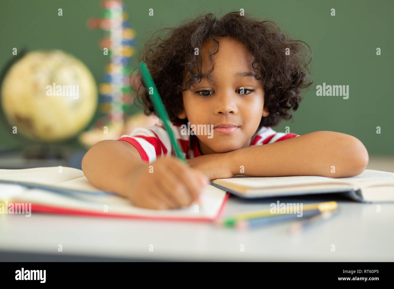 Schoolboy writing on book in a classroom Stock Photo - Alamy