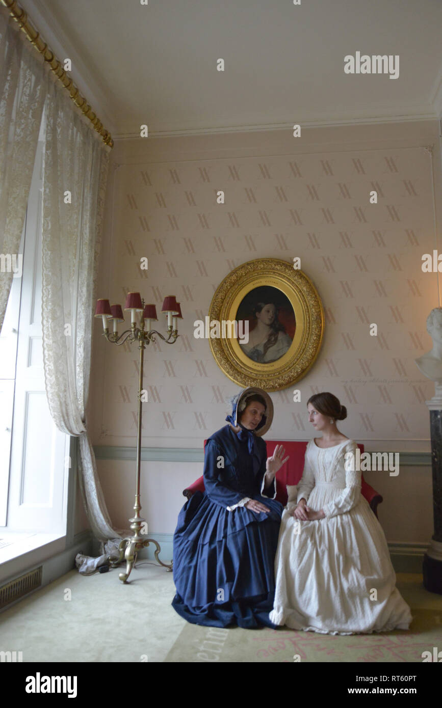 Two Women in Victorian dresses sit and chat in a formal parlour at ...