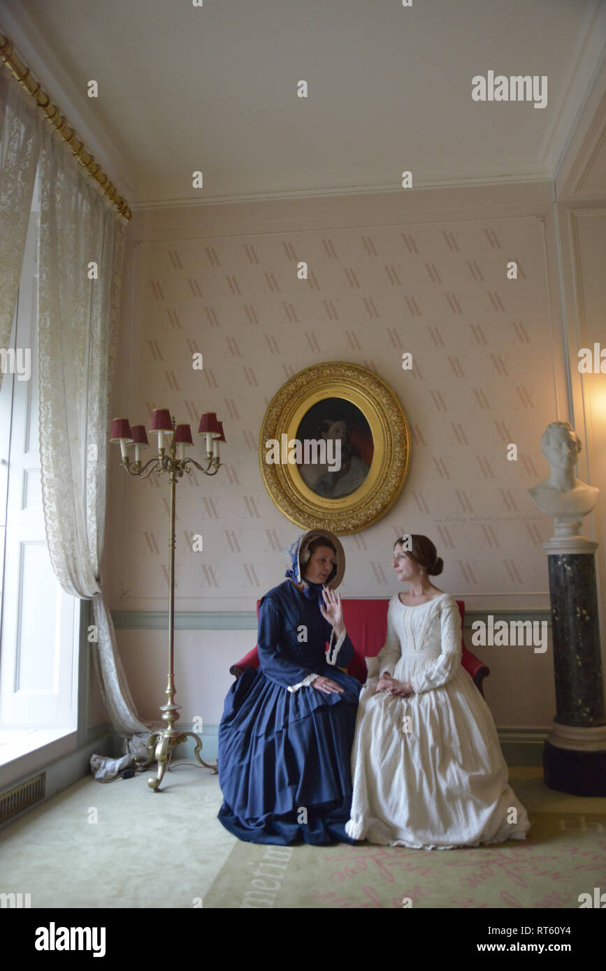 Two Women in Victorian dresses sit and chat in a formal parlour at ...